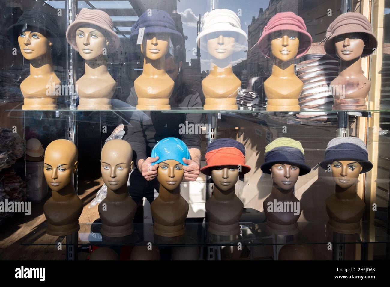 A shopkeeper fits and adjusts the hats on female mannequin heads in the ...