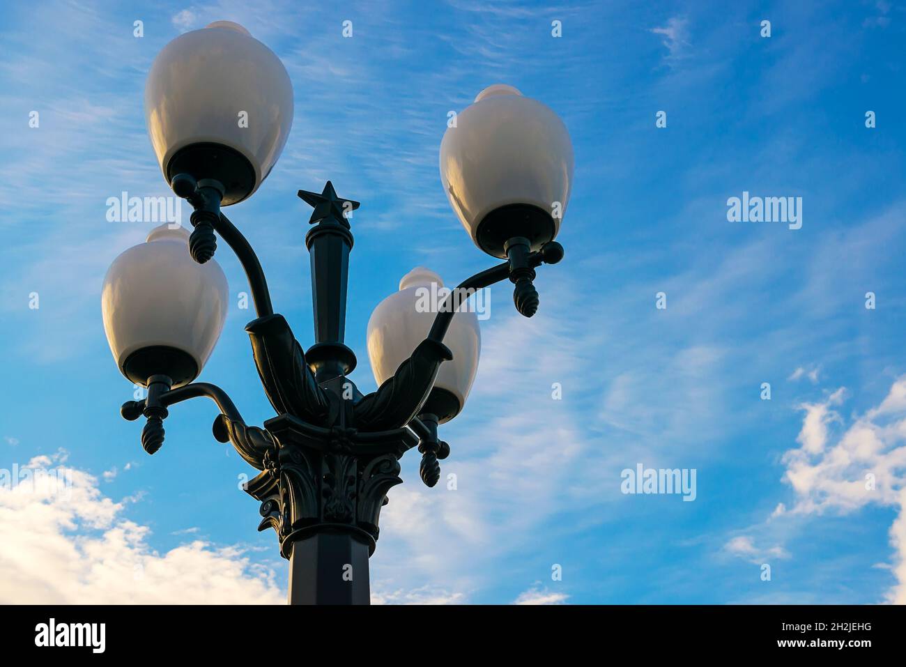 A pillar with four lamps. A lamppost against the sky with white clouds ...