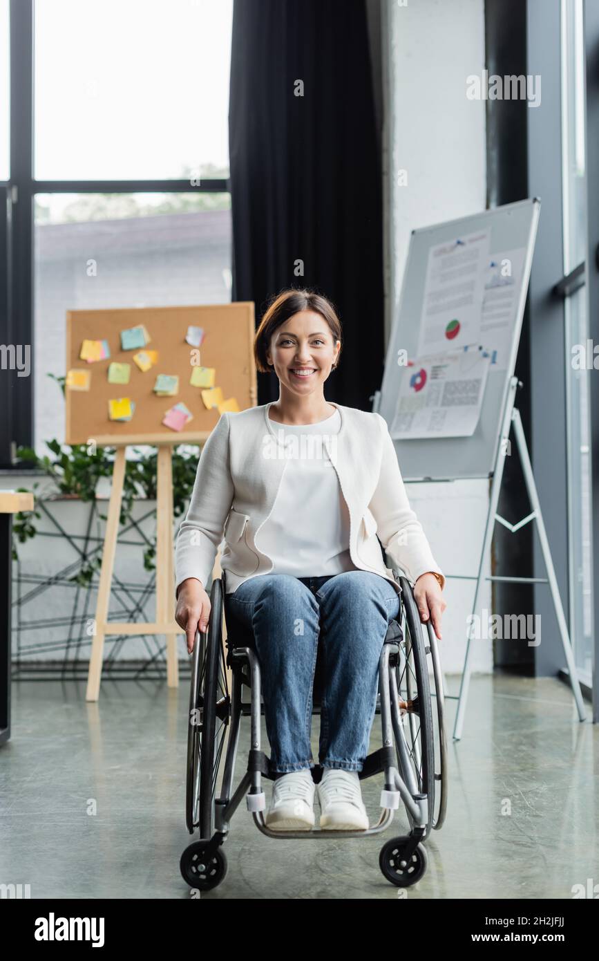 happy businesswoman with physical disability near blurred flip chart ...