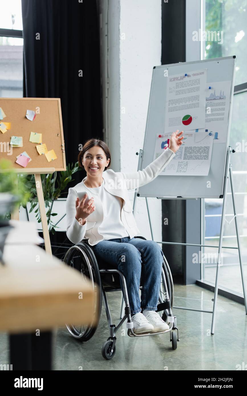 cheerful businesswoman with disability holding smartphone while ...