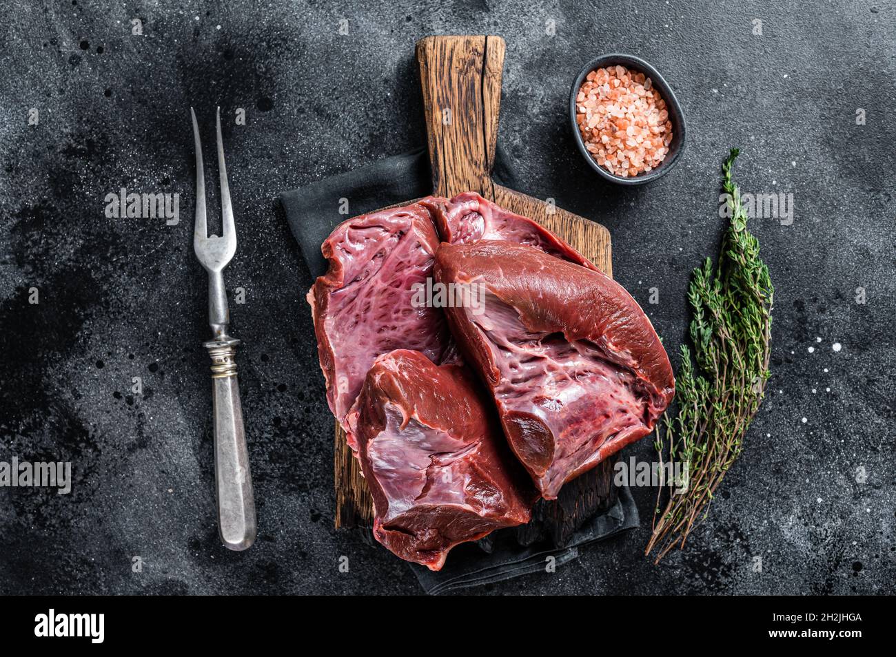 Raw cutted Beef or veal heart on a butcher board. Black background. Top ...