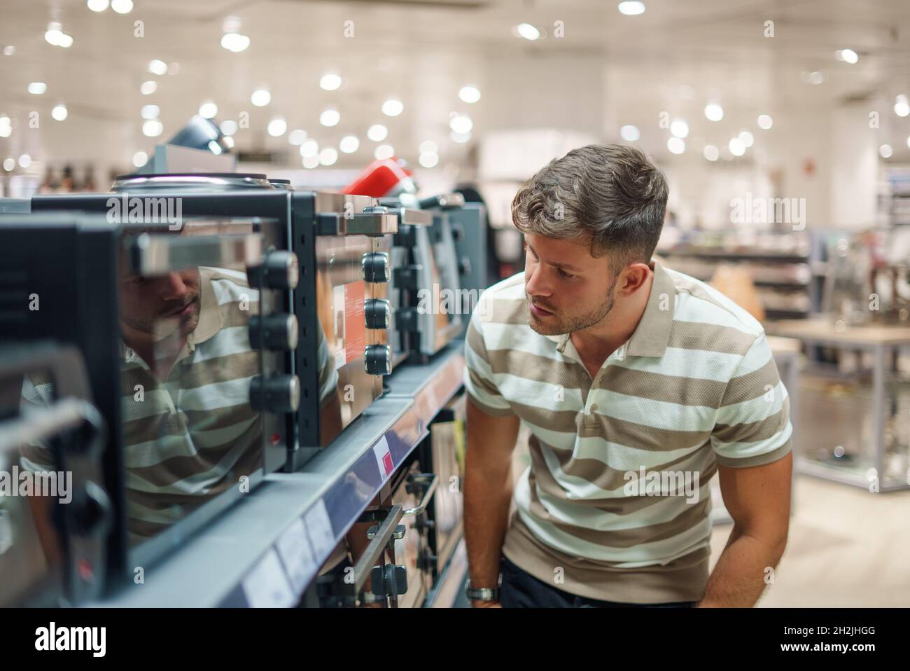 Man in casual clothes looking closely at new microwaves ovens on shelf ...