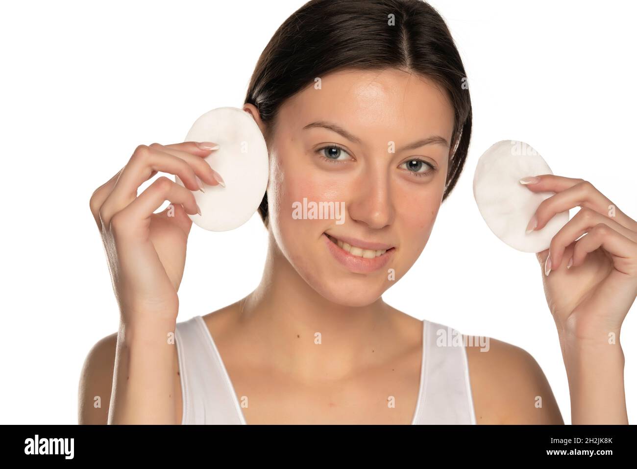 a young smiling woman posing with cotton pads on a white background ...