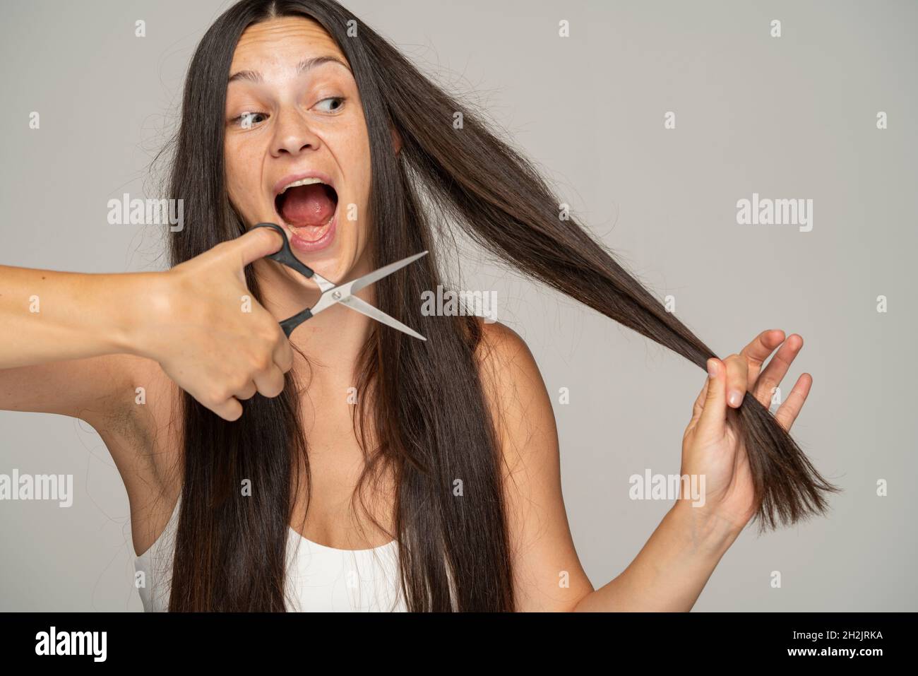 funny woman cuts her hair with scissors on a gray background Stock ...