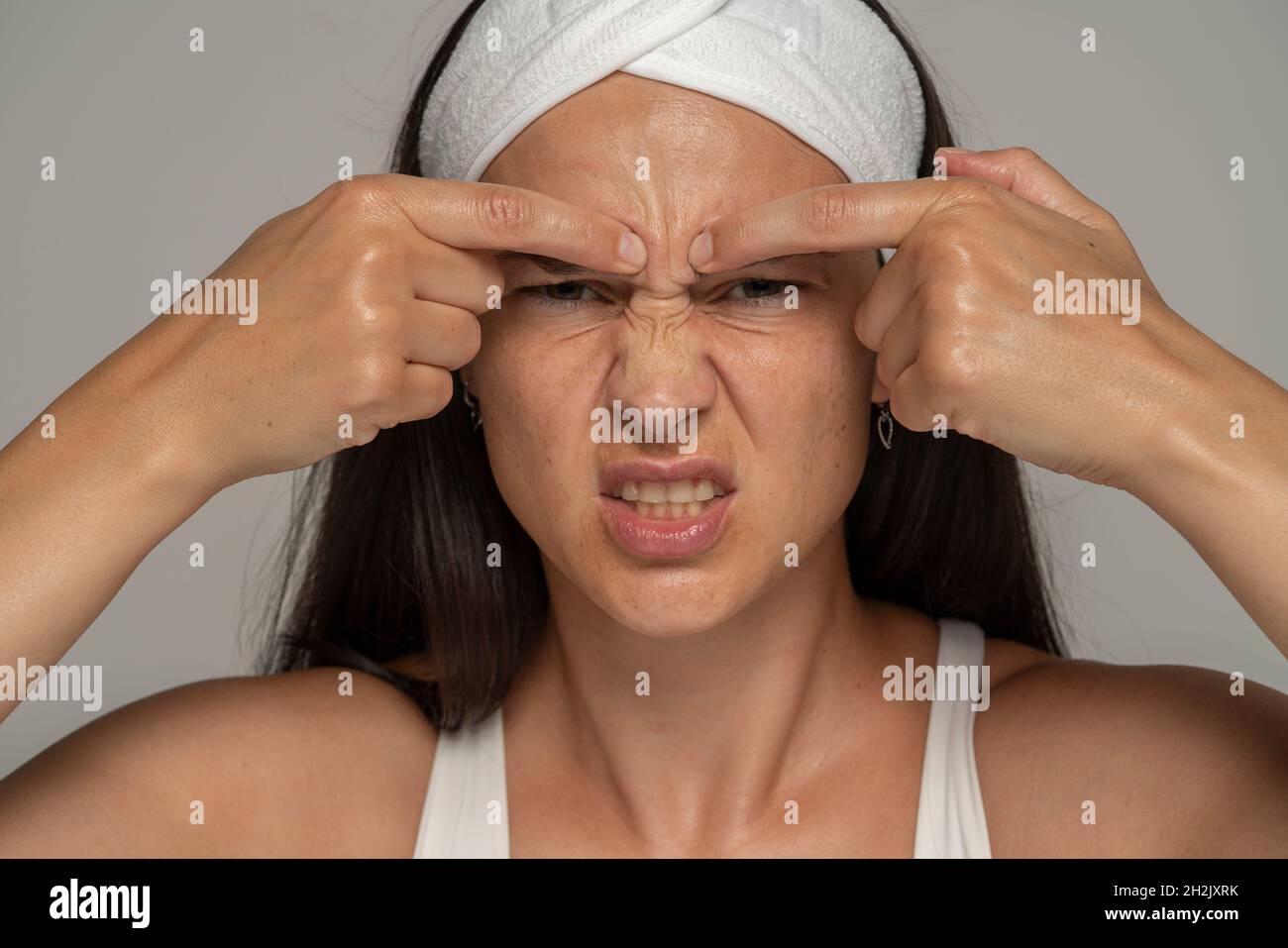 a young frowning woman squeezing a wrinkle on her forehead on a gray ...