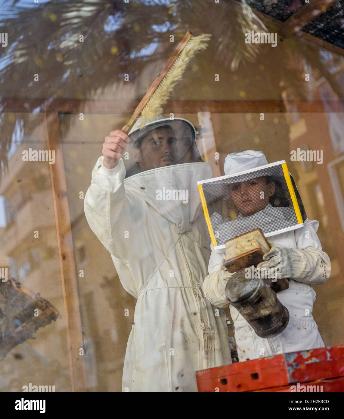 Adult beekeeper showing a comb brush and girl holding a bee smoker ...