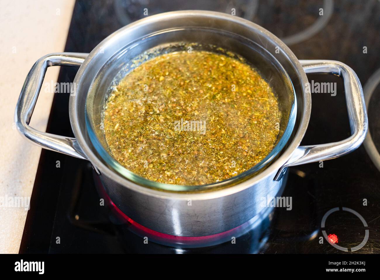 cooking medicinal herbs and plants in water bath on ceramic hob at home ...