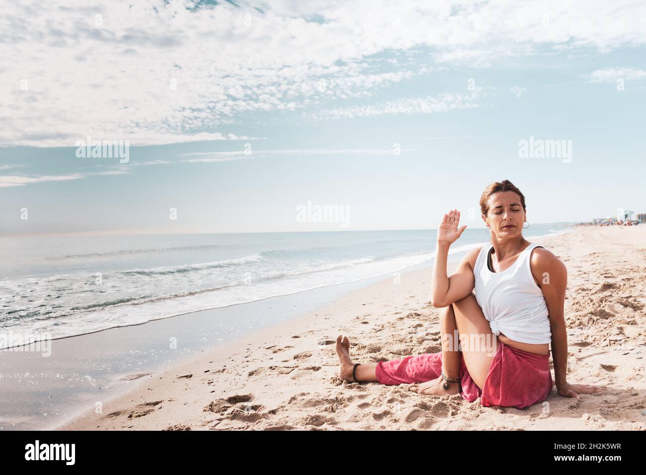 Woman on the beach doing Marichyasana c asana, or marichi sage pose ...