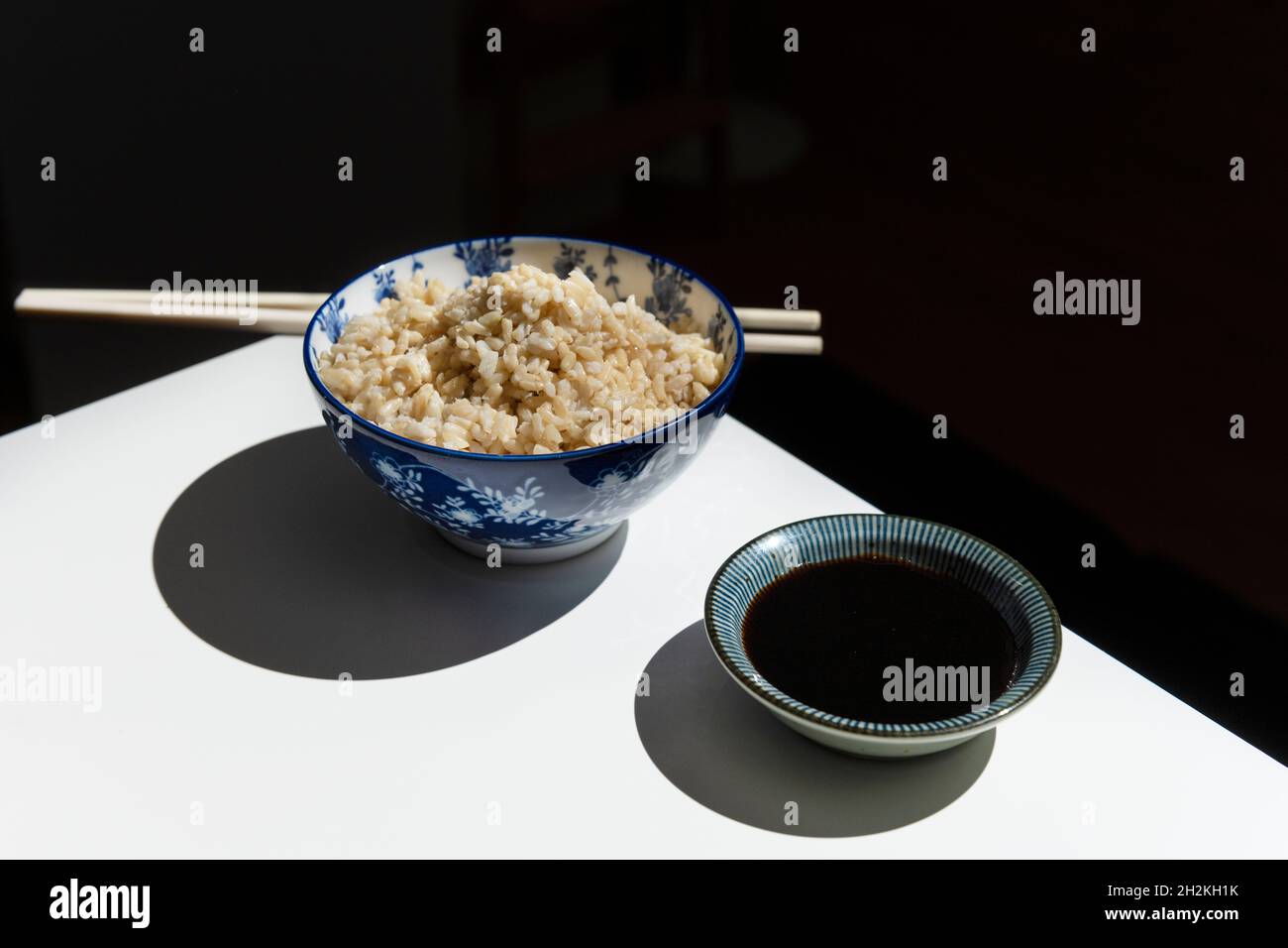 Bowl of cooked rice with soy sauce, chopsticks on white table Stock ...