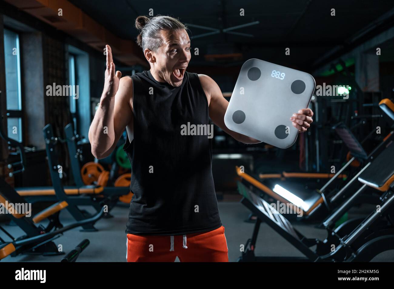 shocked and frustrated man weighing with scale in gym after dieting ...