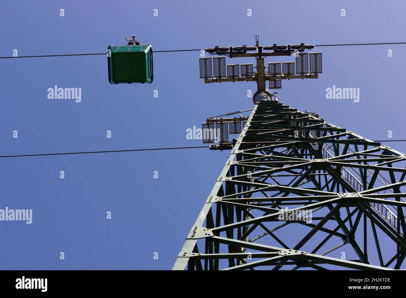 Green cable car by metal tower from below. Tourist attraction concept ...