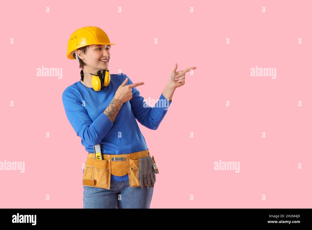 Female construction worker with hardhat and ear protectors on pink ...