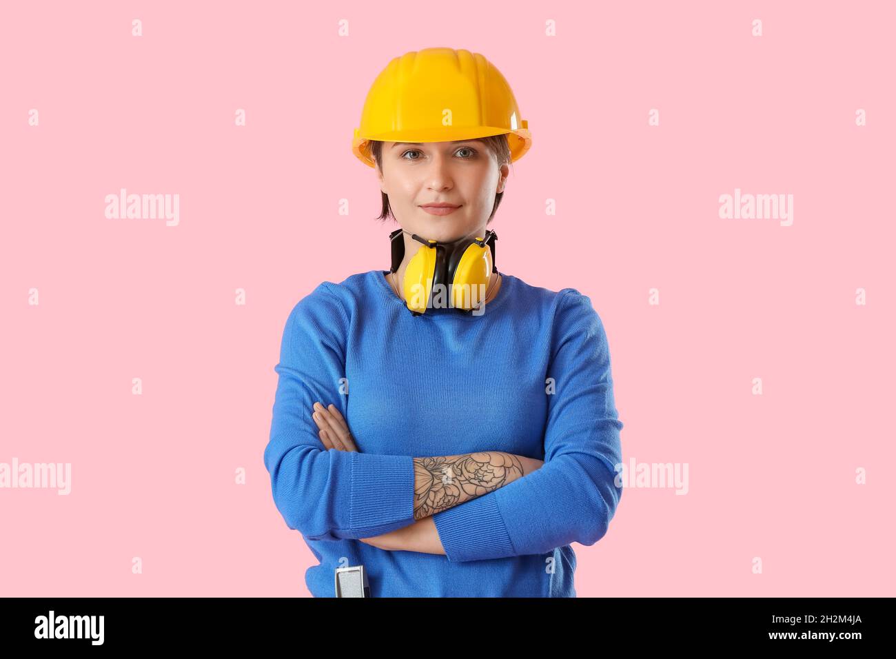 Female construction worker with hardhat and ear protectors on pink ...