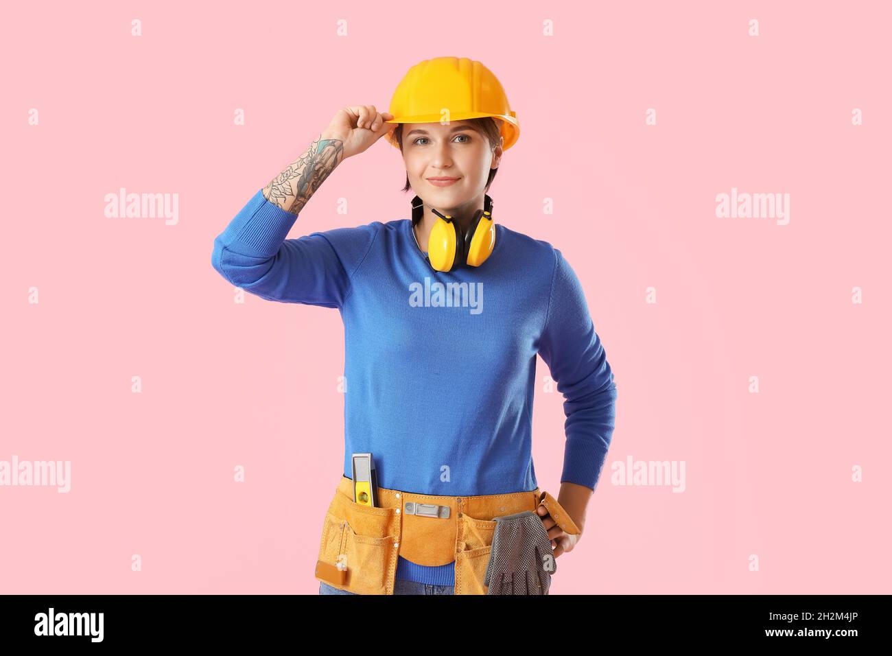 Female construction worker with hardhat and ear protectors on pink ...