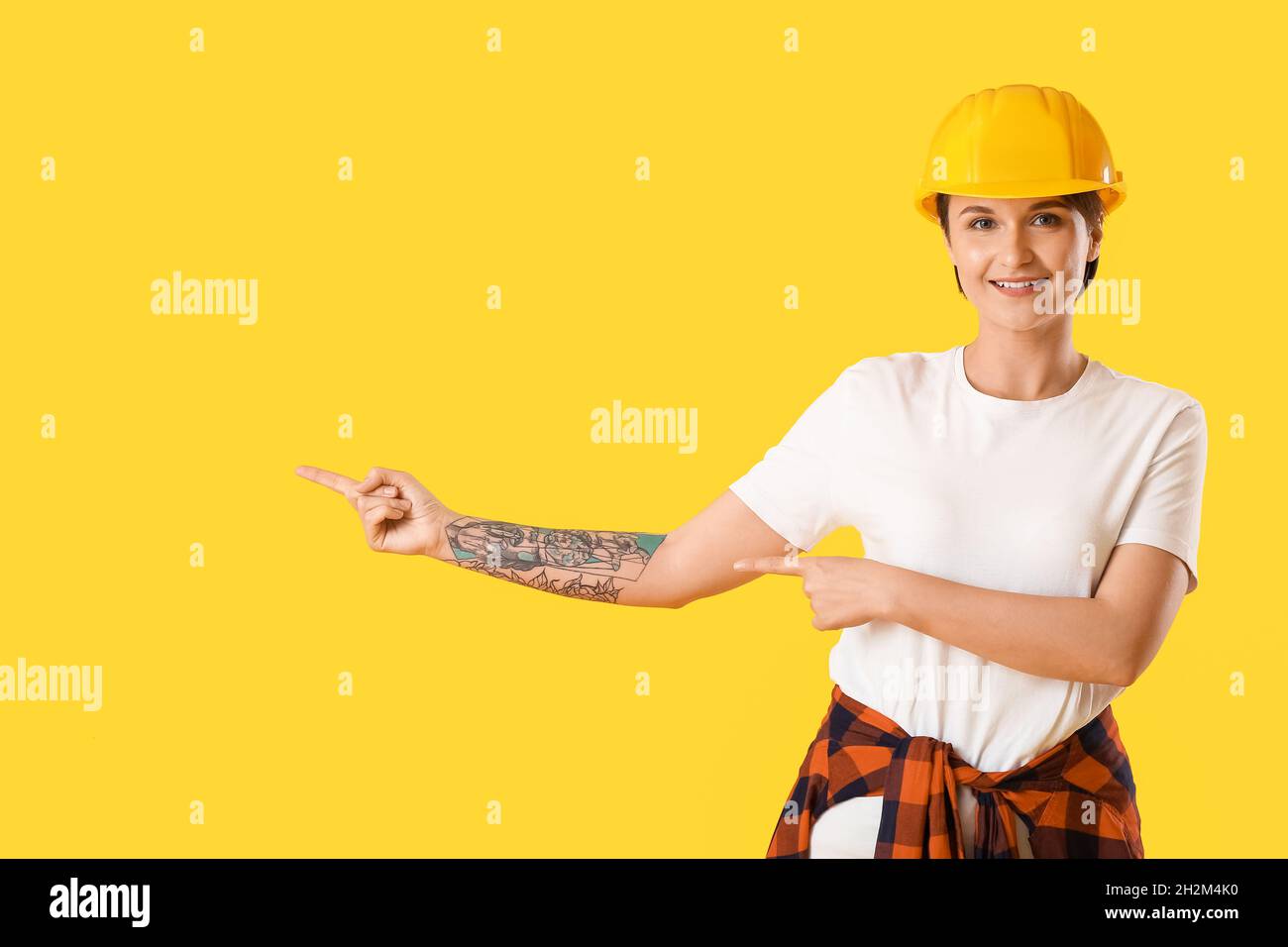 Female construction worker in hardhat pointing at something on yellow ...