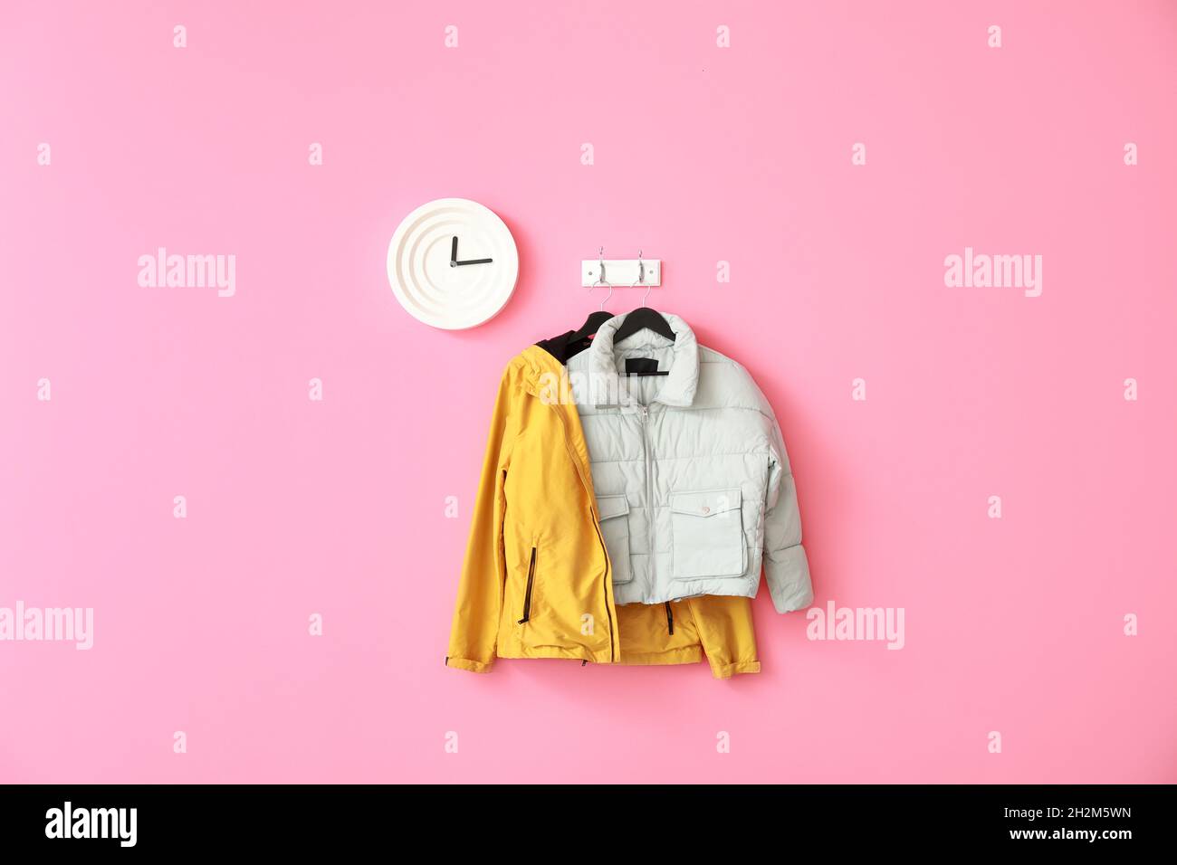 Stylish jackets and clock hanging on pink wall Stock Photo - Alamy