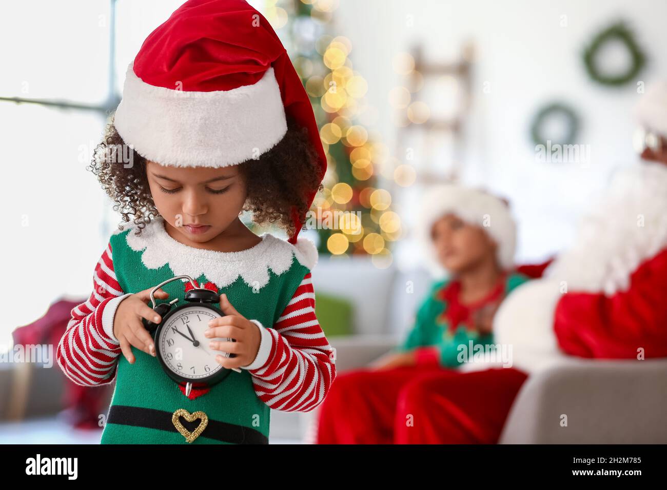Little African-American girl dressed as elf with alarm clock at home ...