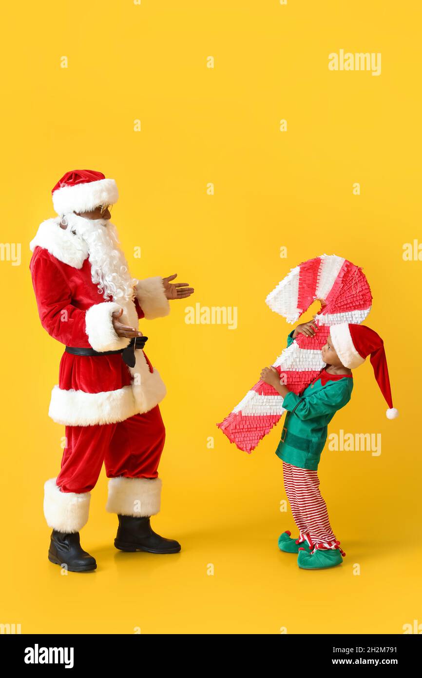 Cute little elf with candy cane pinata and Santa Claus on yellow ...