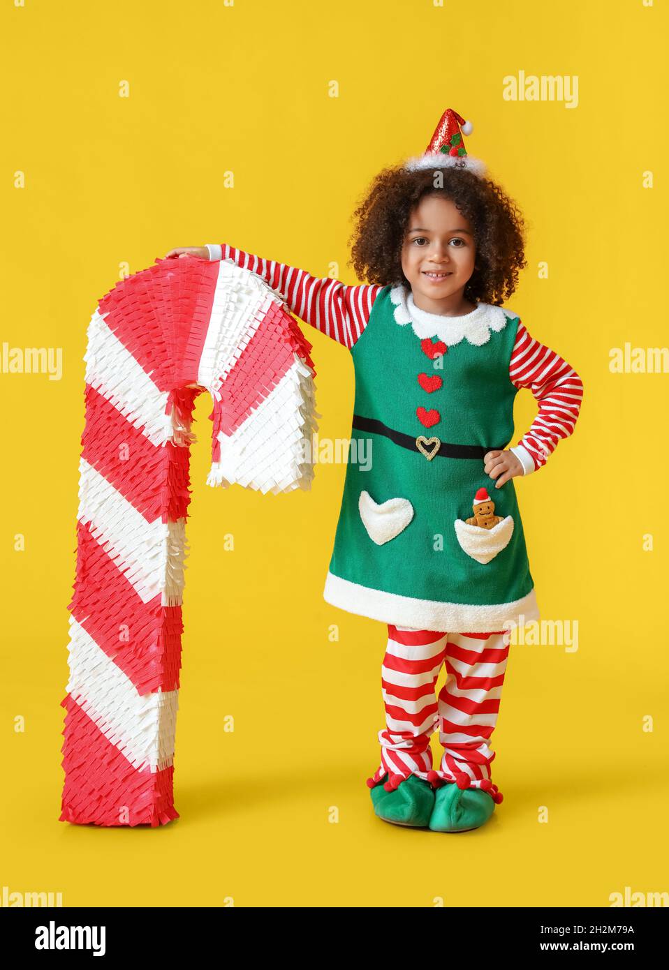 Cute little elf with candy cane pinata on yellow background Stock Photo ...