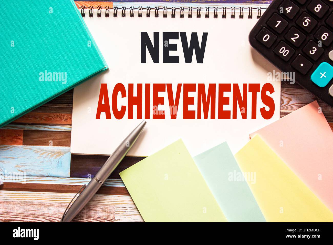 Text New achievements on the white notepad page. Table, top view ...