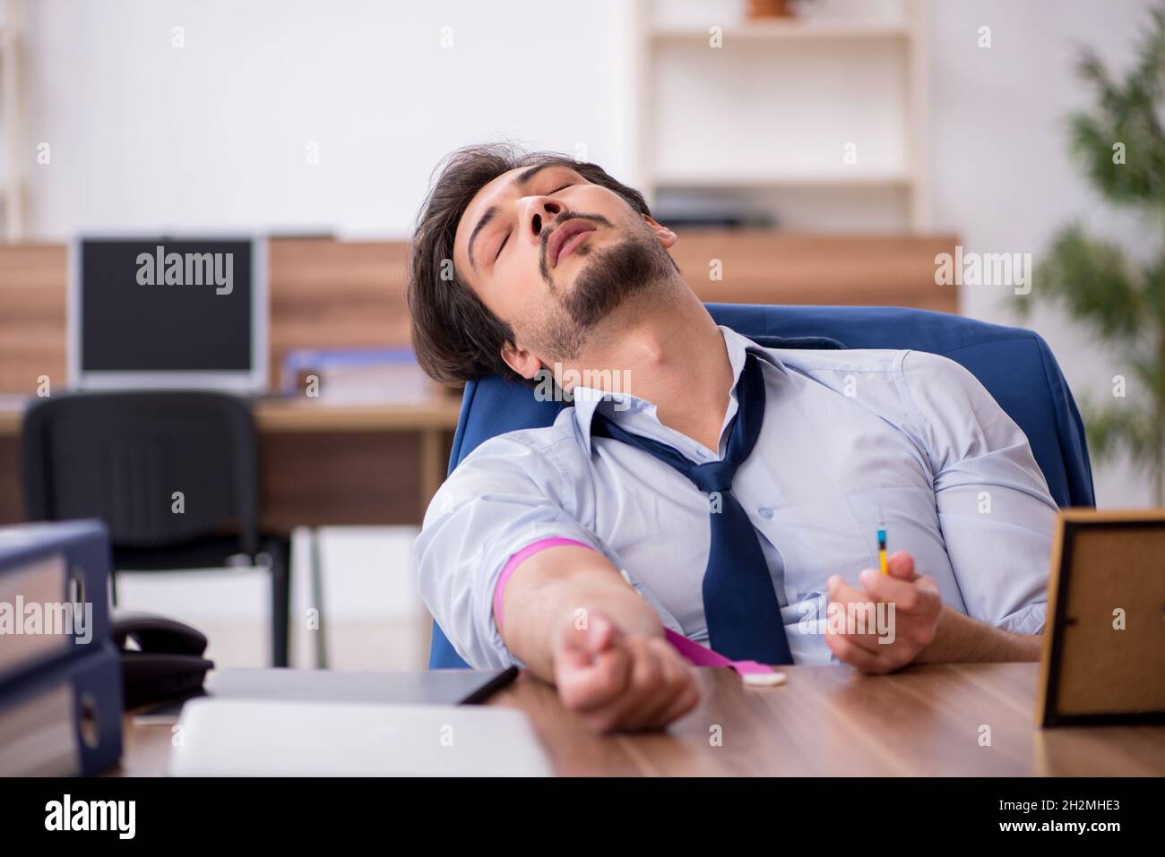 Young male drug addicted employee in the office Stock Photo - Alamy