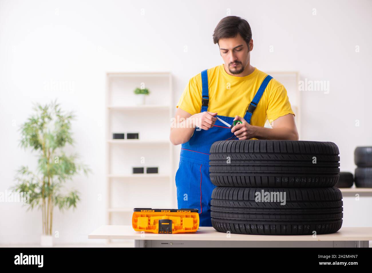 Young garage worker with tyre at workshop Stock Photo - Alamy