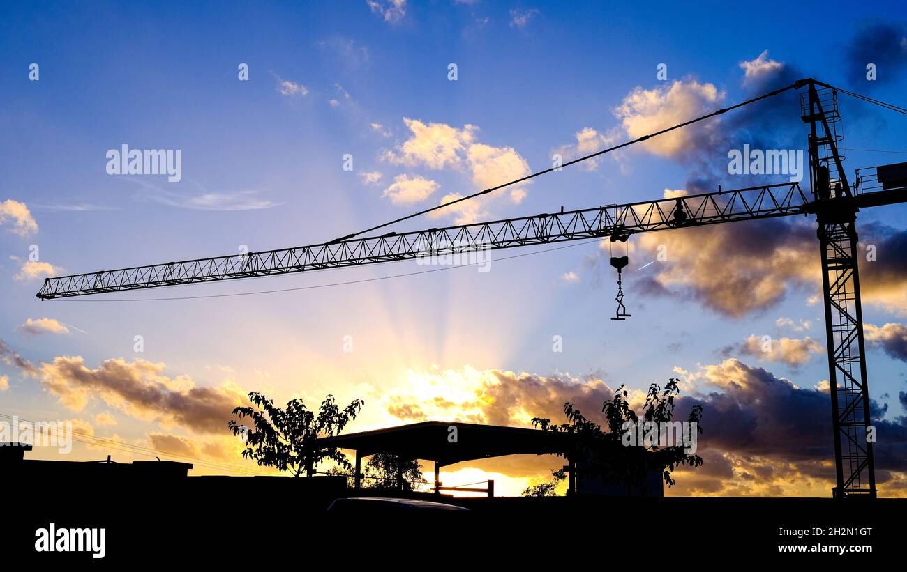 silhouette of crane and roof in backlight with sun behind clouds. end ...