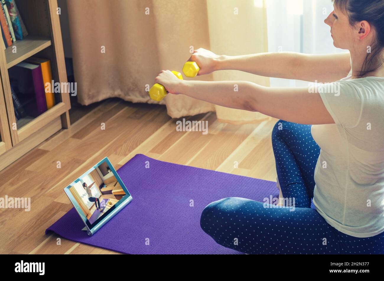 Young woman doing workout sports at home, raising dumbbells with ...