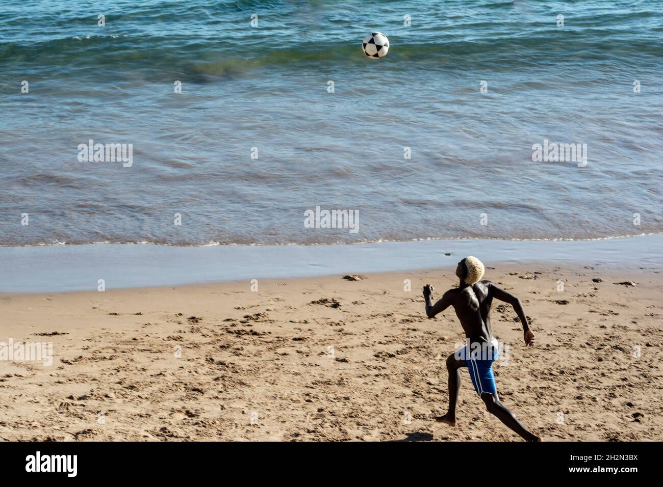 Young model playing sand football on the beach under strong summer sun ...