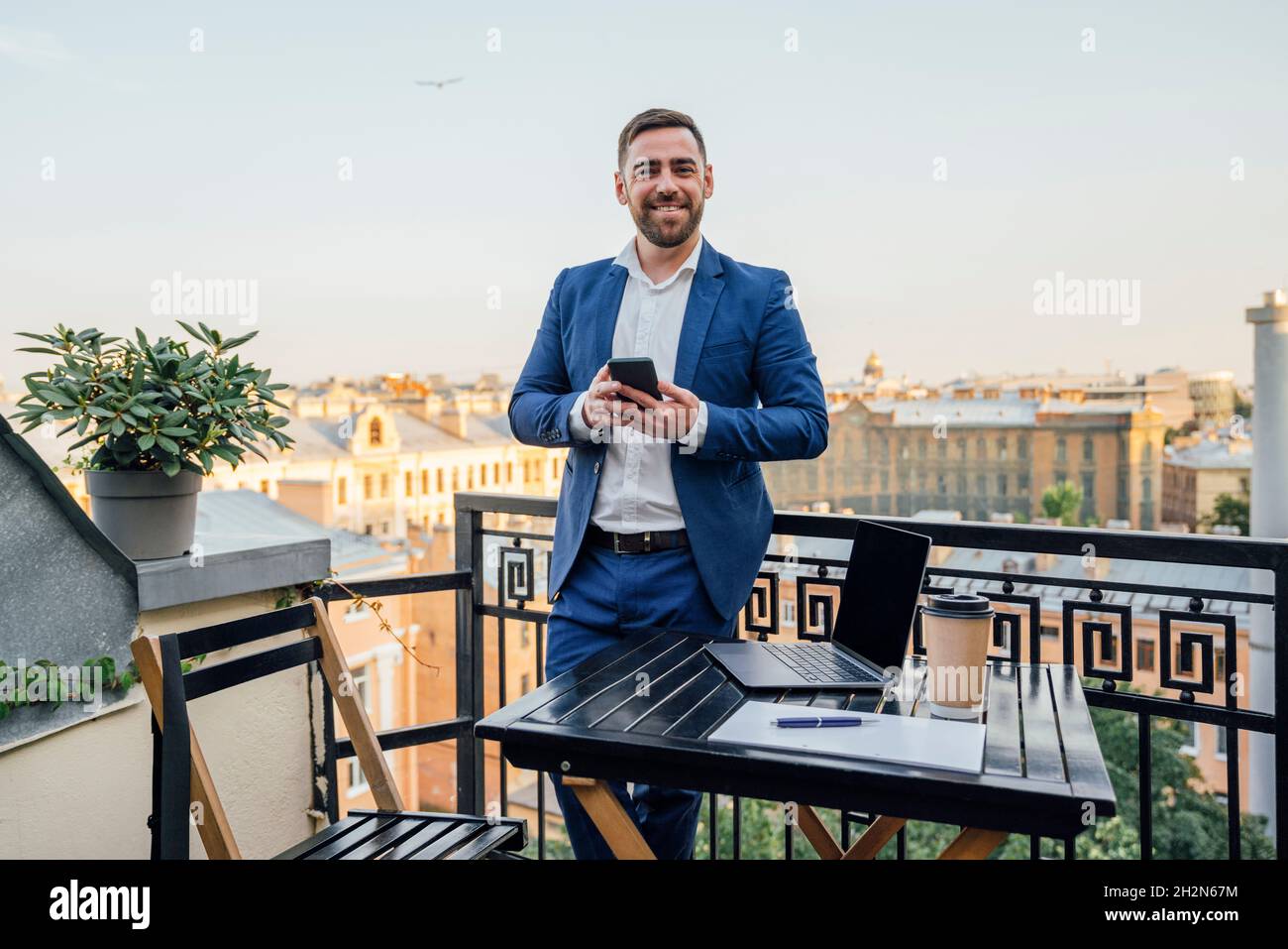 Male business person with smart phone leaning on railing in office ...
