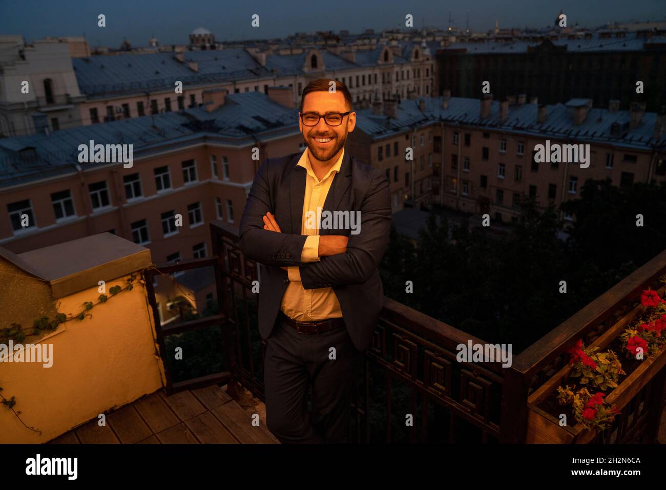 Male professional with arms crossed leaning on railing during night ...