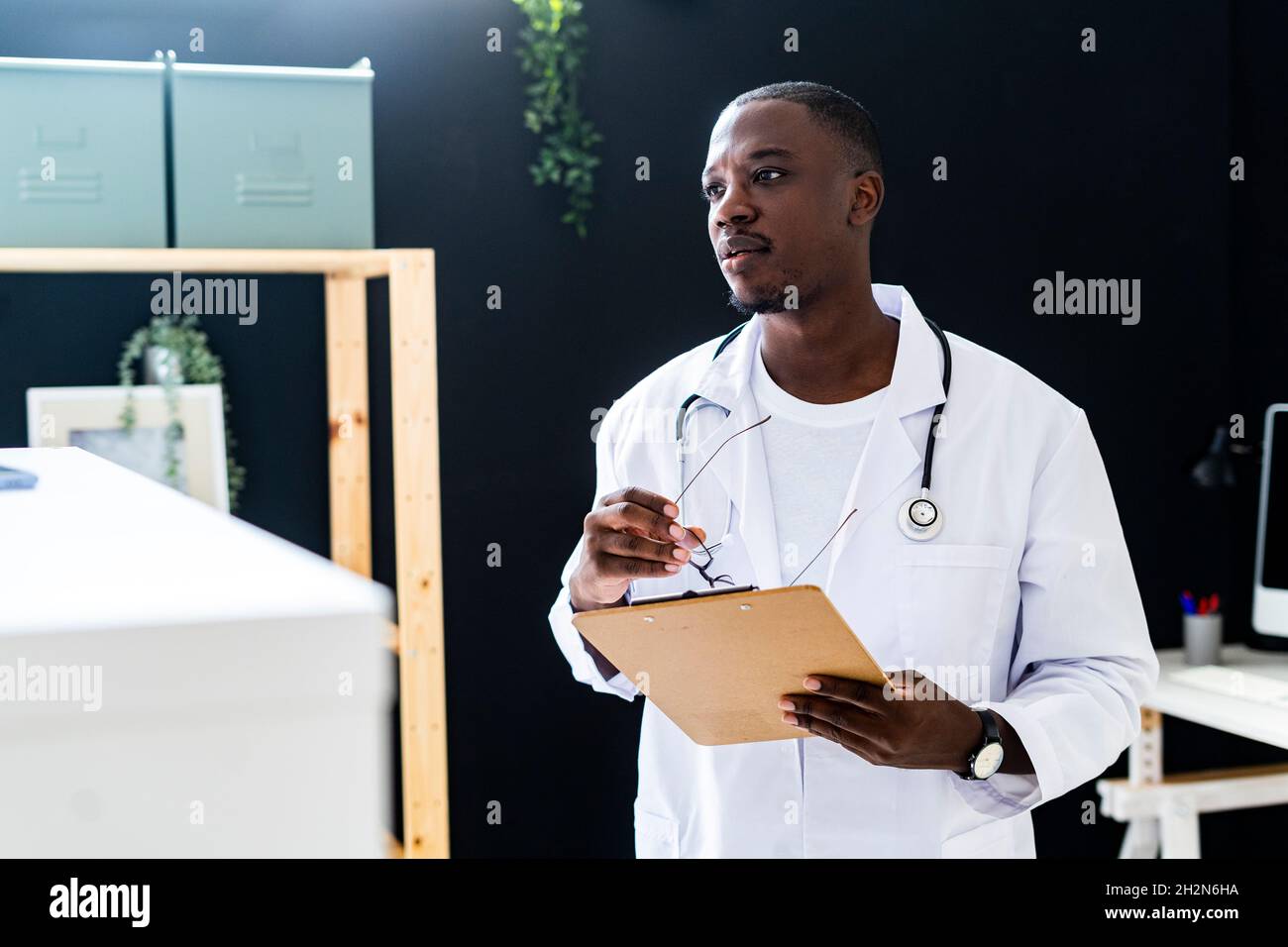 Smiling male doctor in lab coat holding clipboard at medical clinic ...
