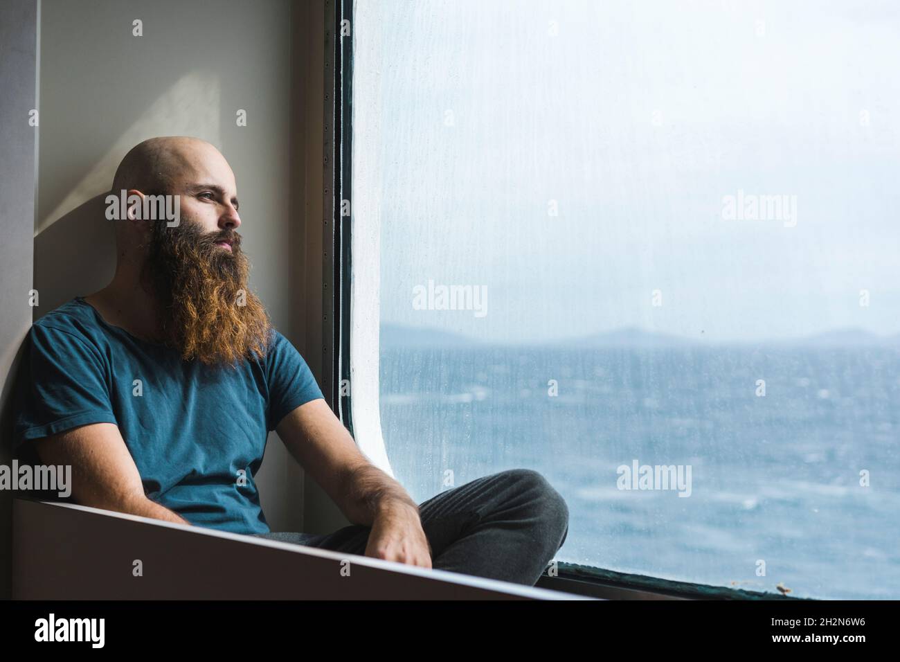 Young bald man looking through glass window Stock Photo - Alamy
