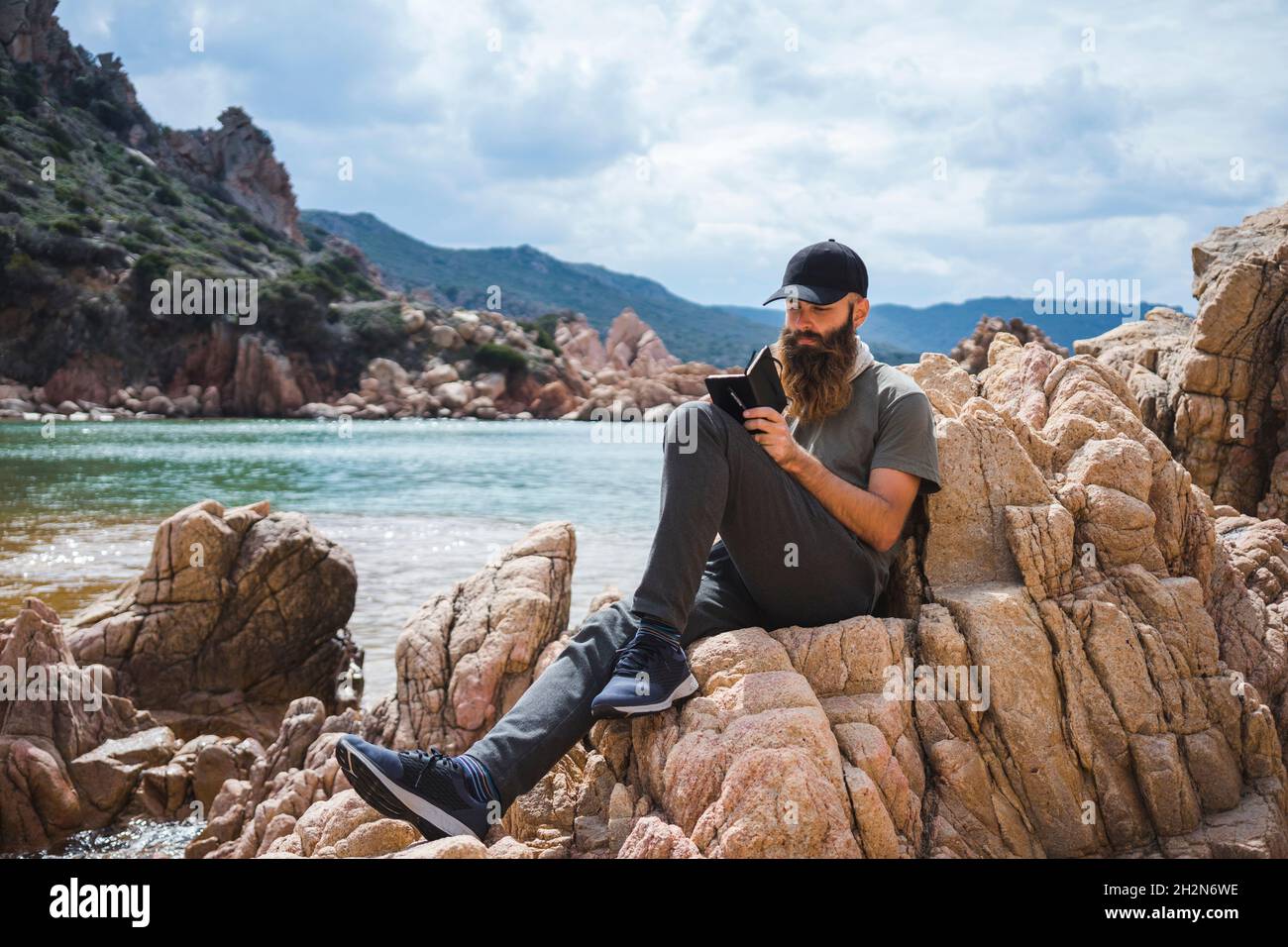 Man writing in book while sitting on rock Stock Photo - Alamy