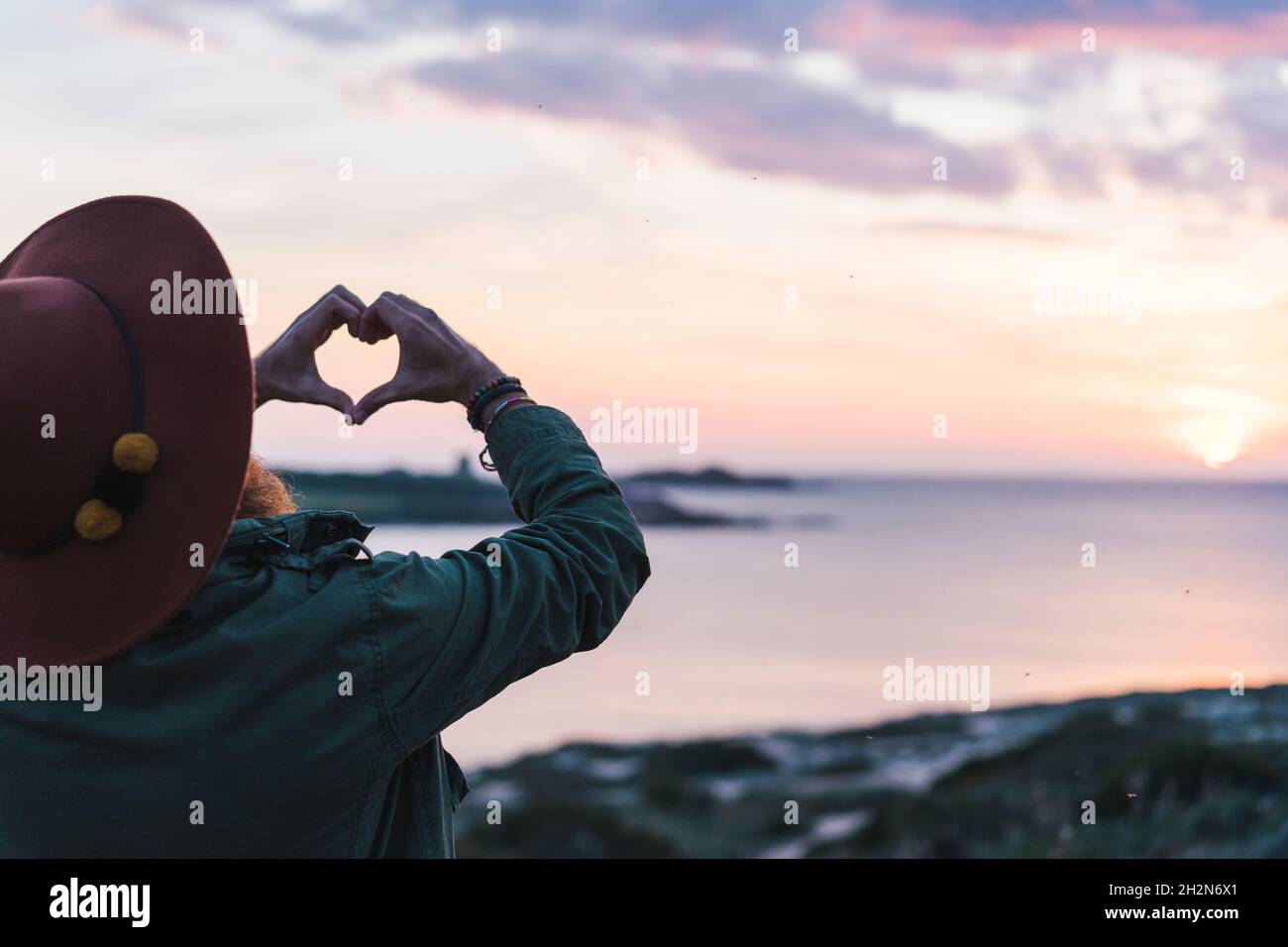 Man wearing hat gesturing heart shape at beach Stock Photo - Alamy