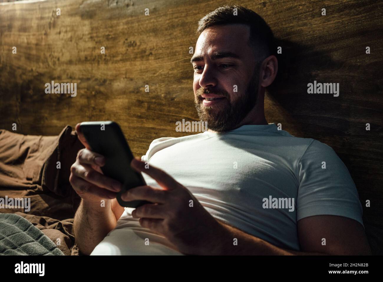 Smiling man using smart phone on bed Stock Photo - Alamy