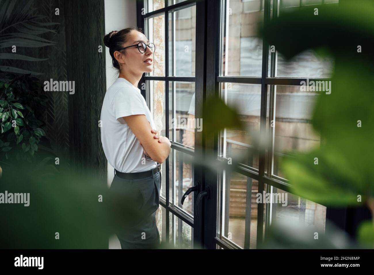 Mid adult businesswoman standing with arms crossed looking through ...
