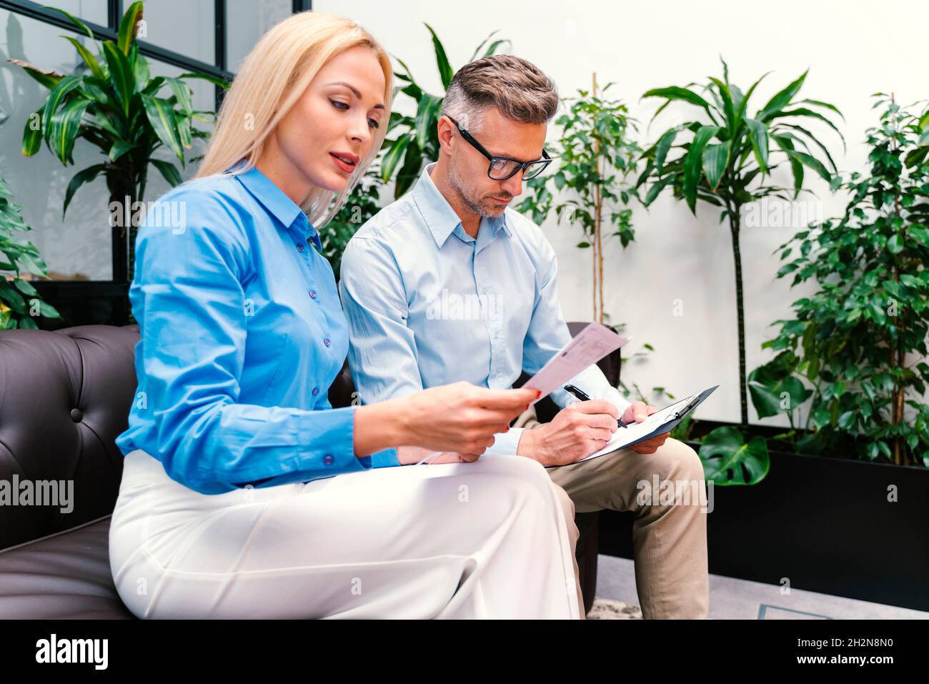 Female professional reading document while sitting by male colleague in ...