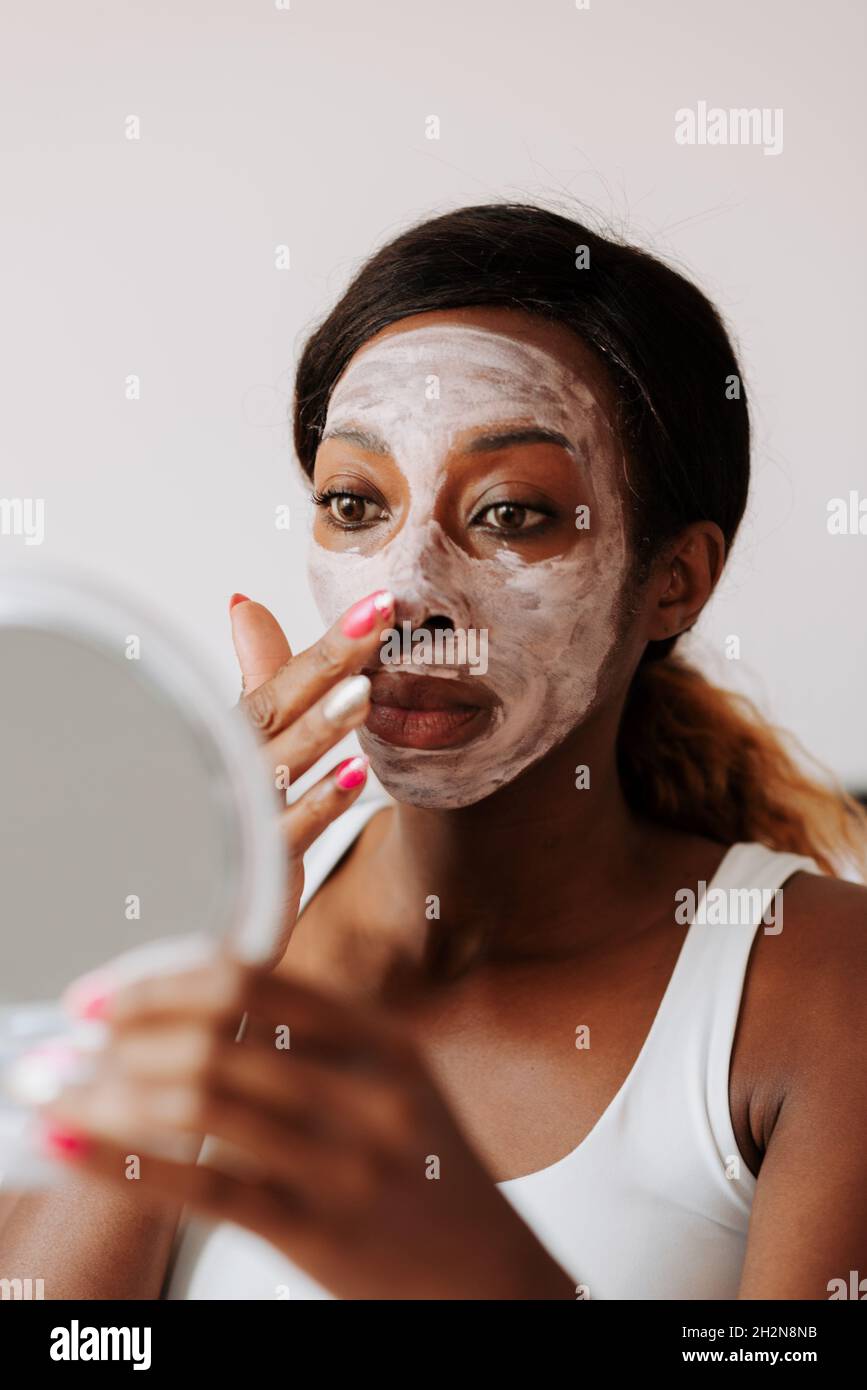 Vertical shot of a black female rubbing the white mask on her face ...