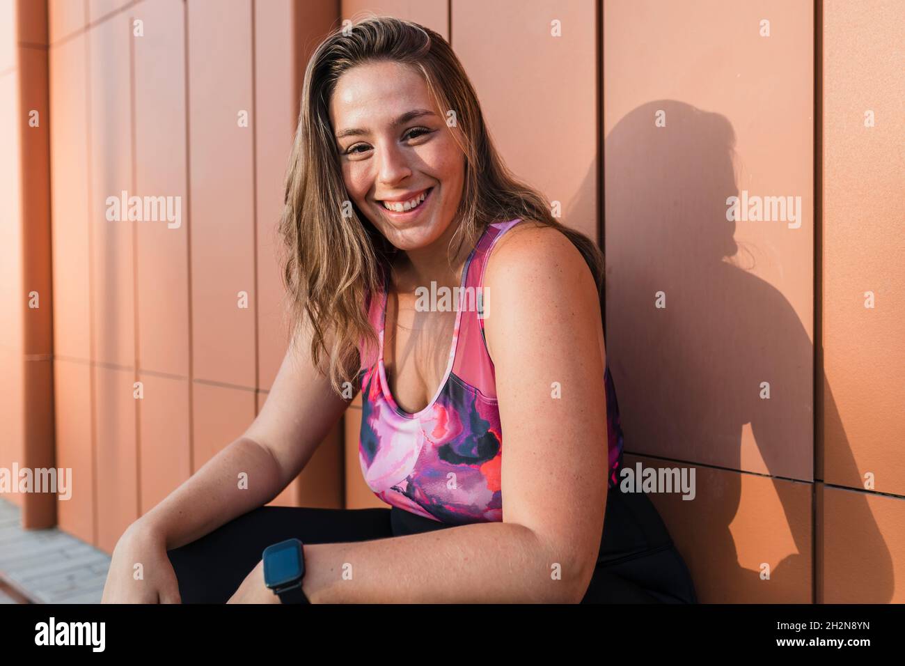 Beautiful smiling woman with brown hair crouching in front of wall ...