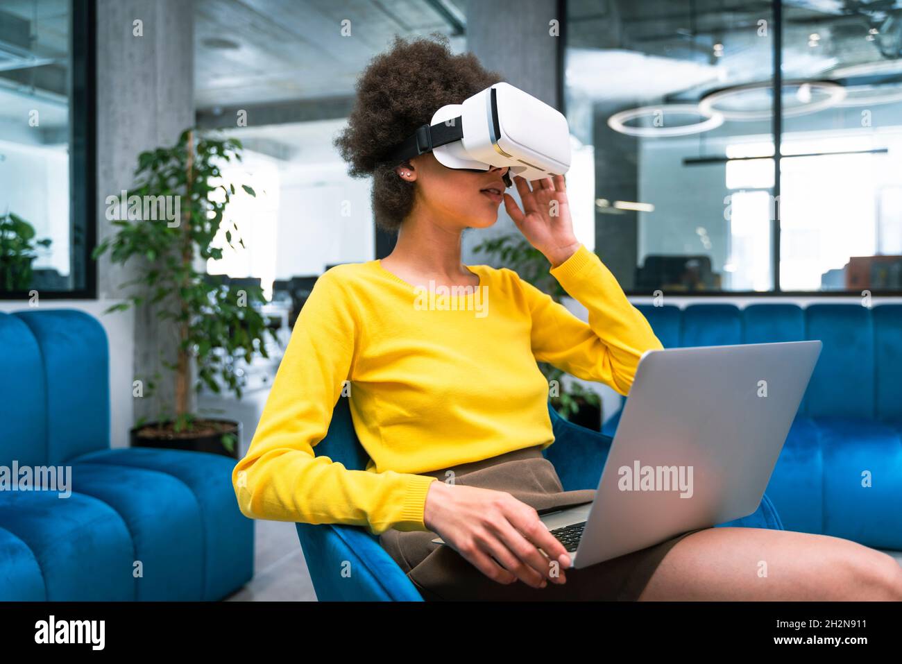 Businesswoman with laptop wearing virtual reality headset while sitting ...