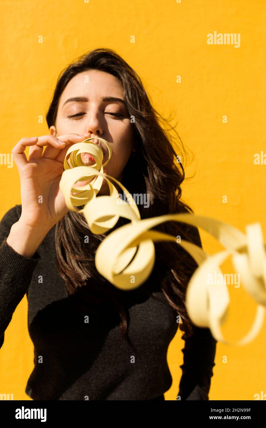 Young woman blowing party blower in front of yellow wall Stock Photo ...