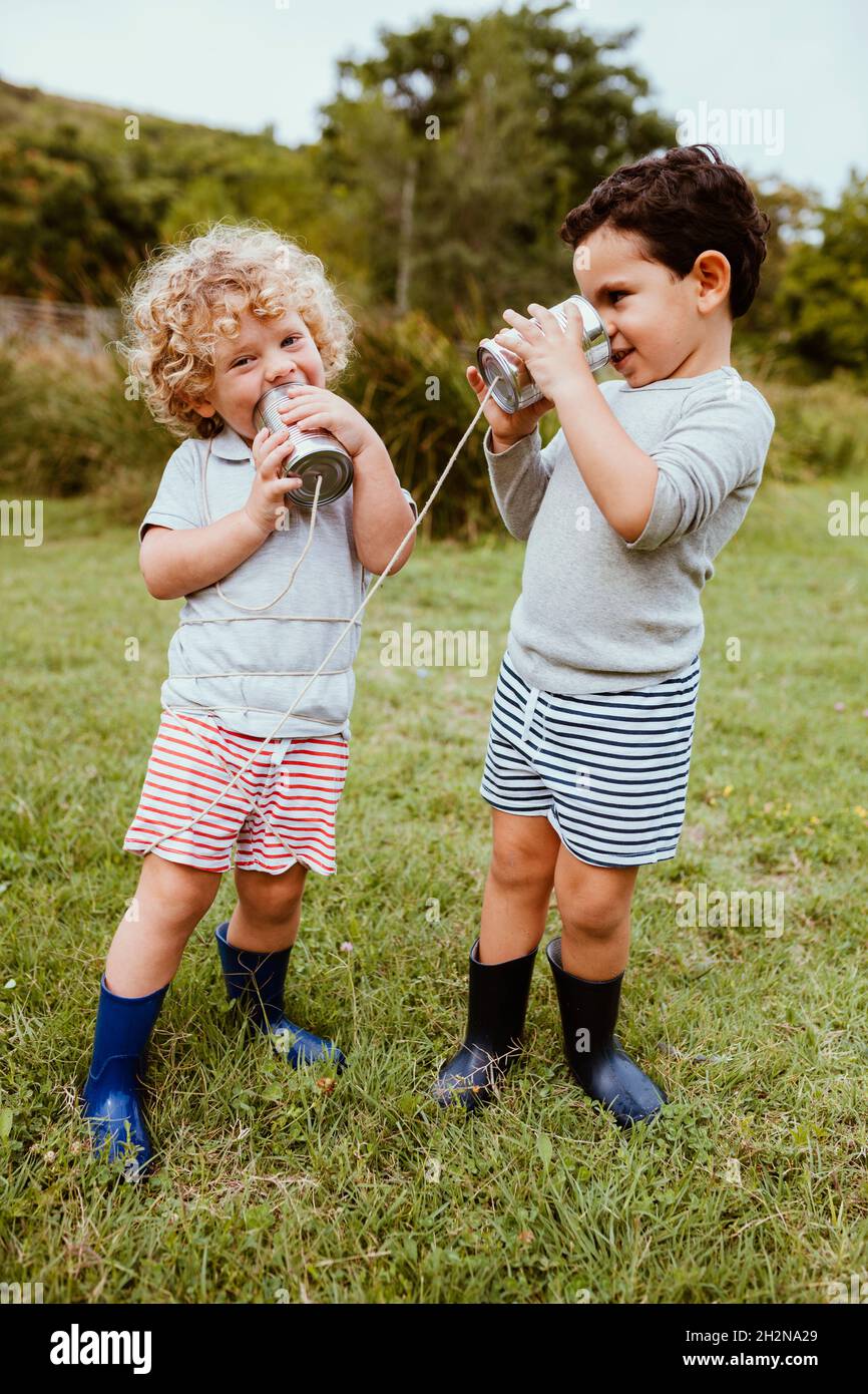 Happy male friends talking through tin can phone while playing on ...