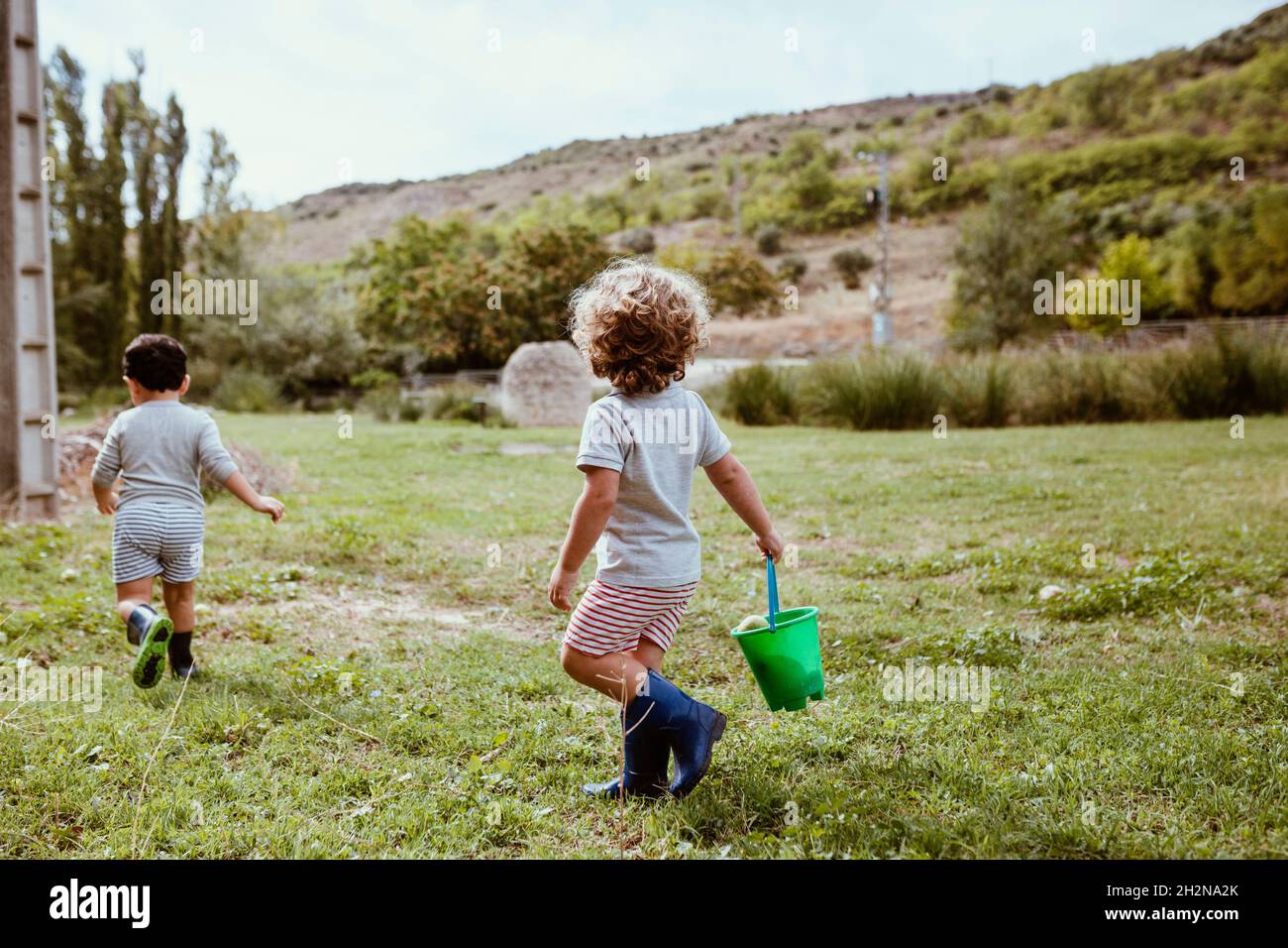 Boy carrying bucket while running with male friend on meadow Stock ...