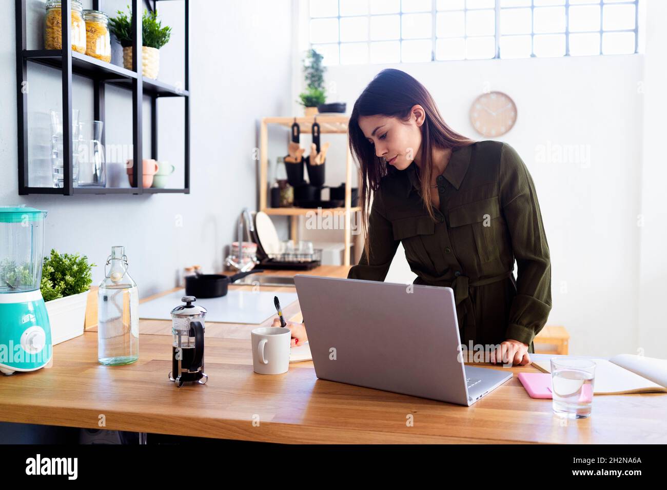Female freelancer writing while standing at kitchen counter Stock Photo ...