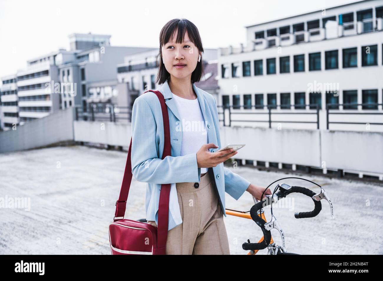 Female teenager with mobile phone wheeling bicycle on parking garage ...
