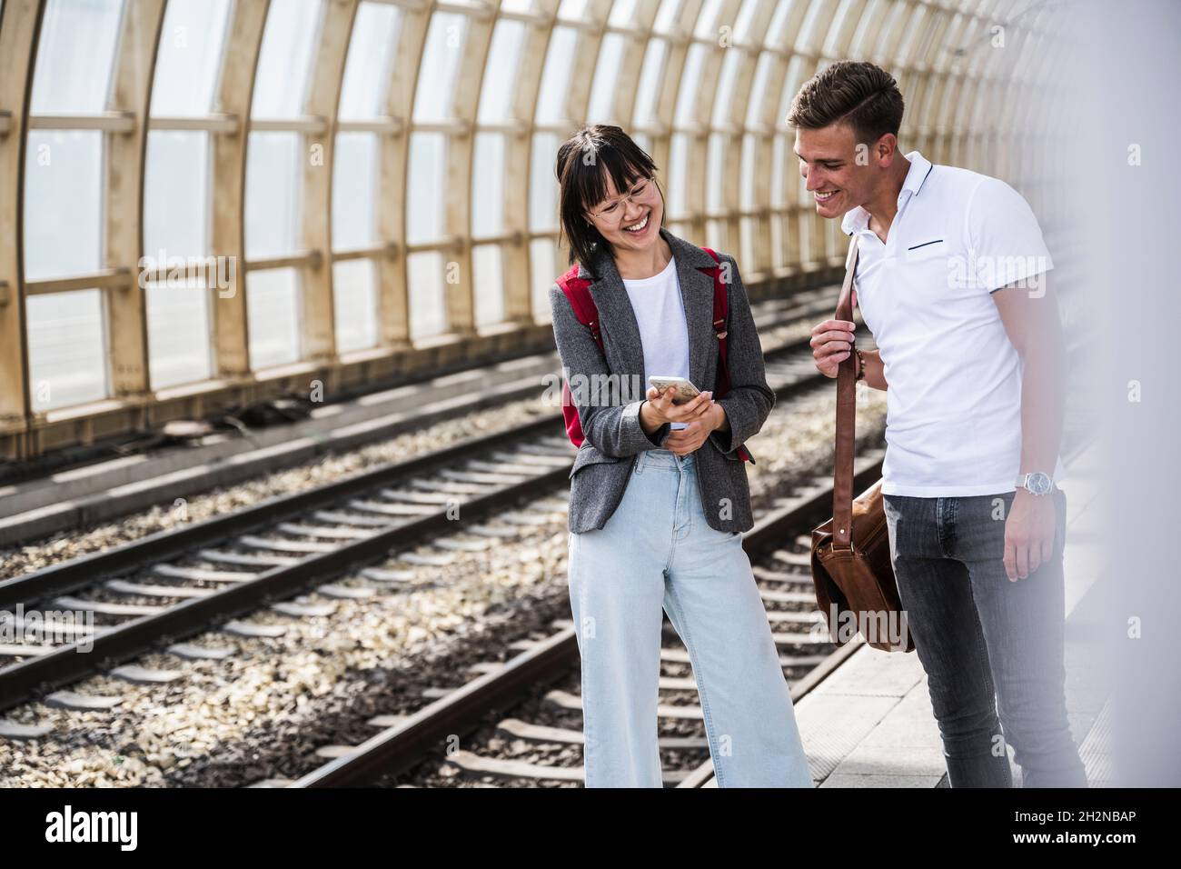 Happy male and female friends sharing mobile phone at train station ...