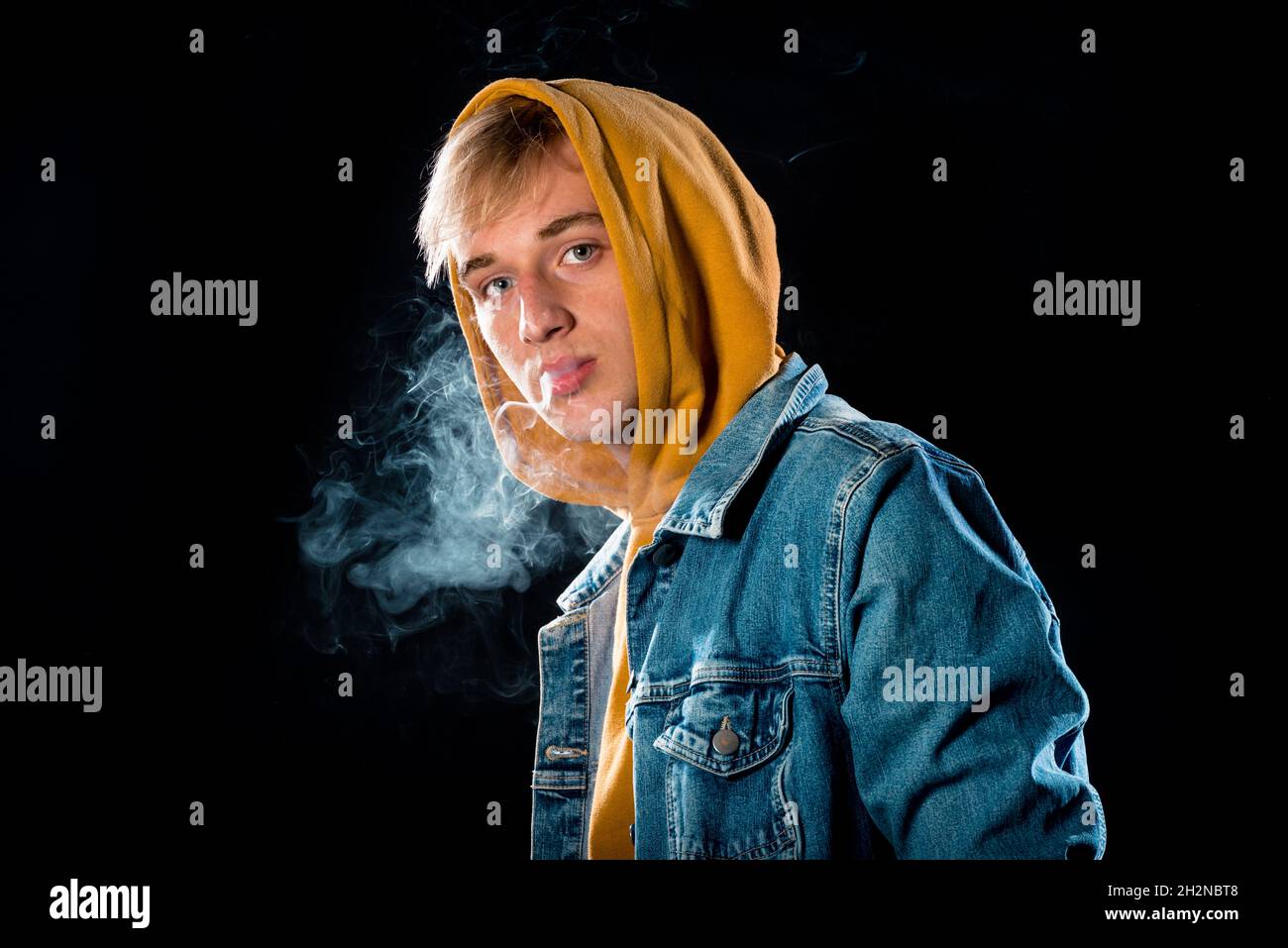 Trendy handsome man smoking cigarette and posing in trendy denim jacket ...