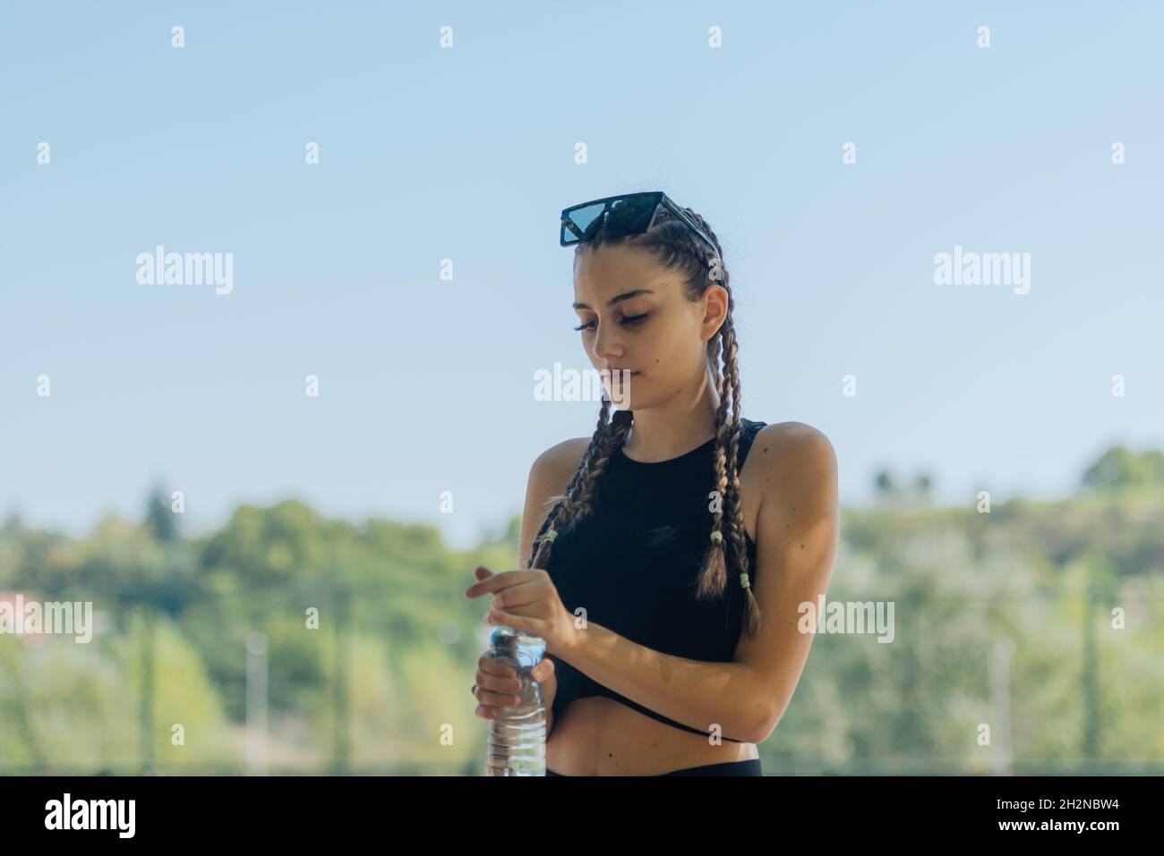 Portrait of a happy female athlete drinking water from a plastic bottle ...