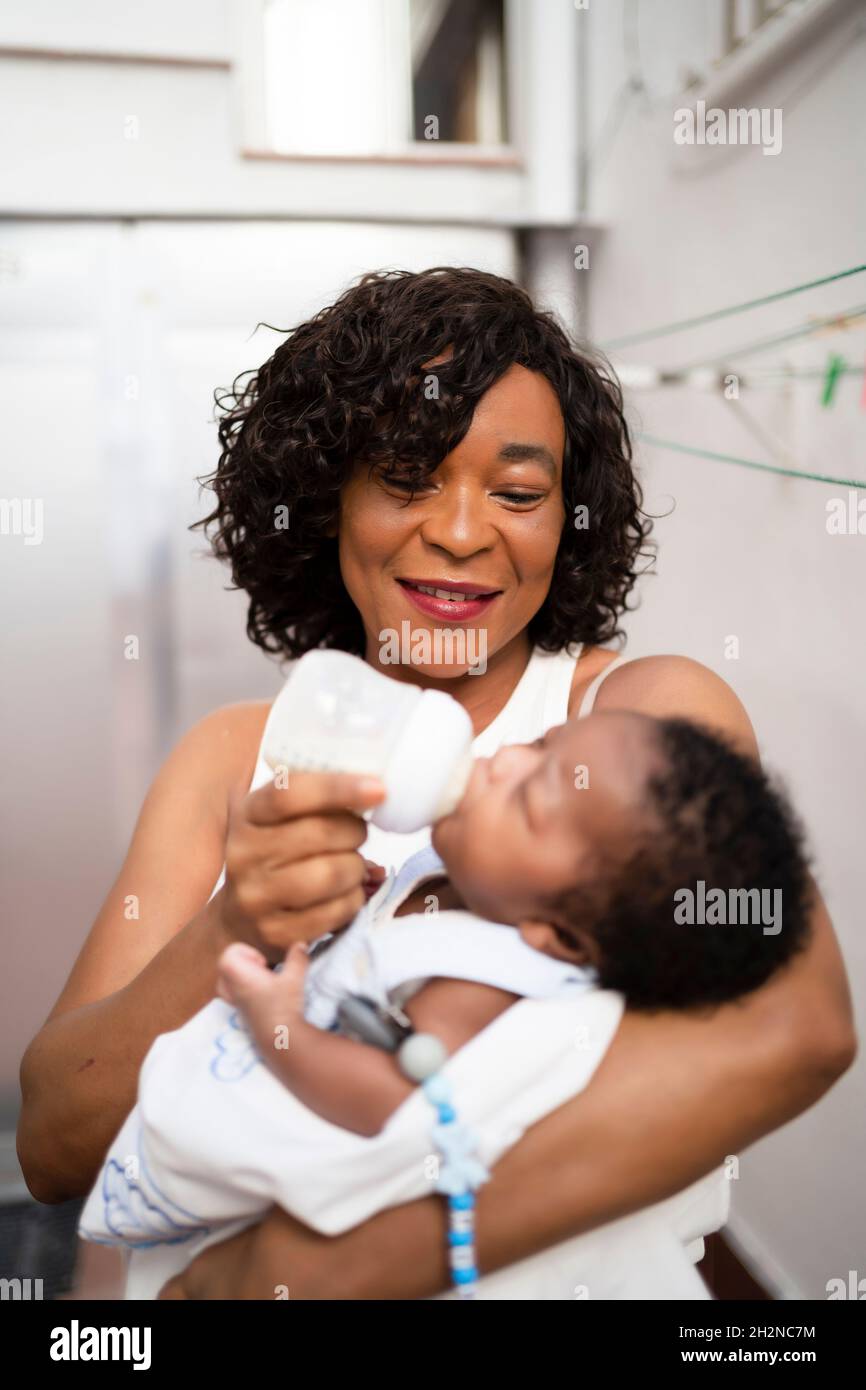Smiling mature woman feeding milk to baby boy at home Stock Photo - Alamy